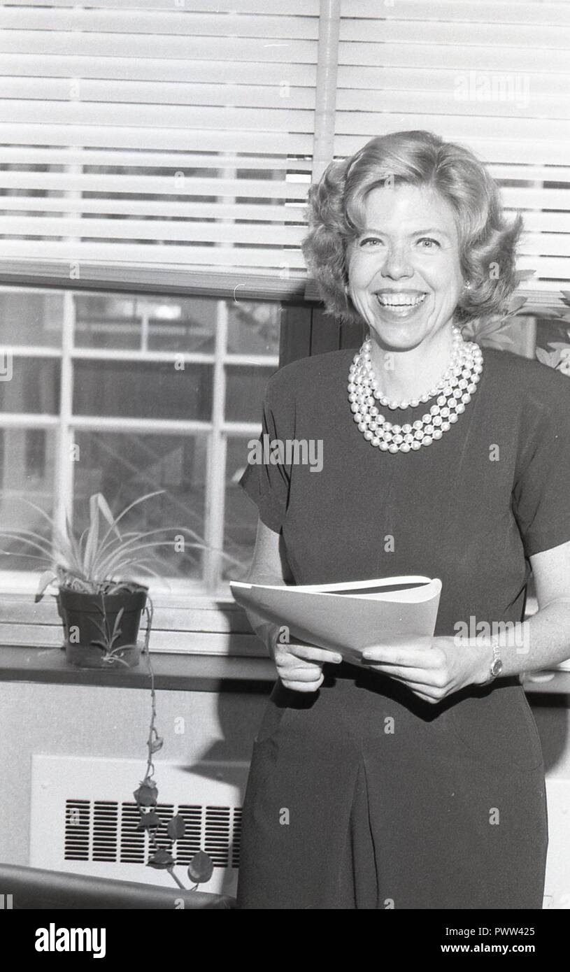 BARBARA UPTON IS STANDING AND SMILING WITH SOME PAPERS IN HER HANDS ...