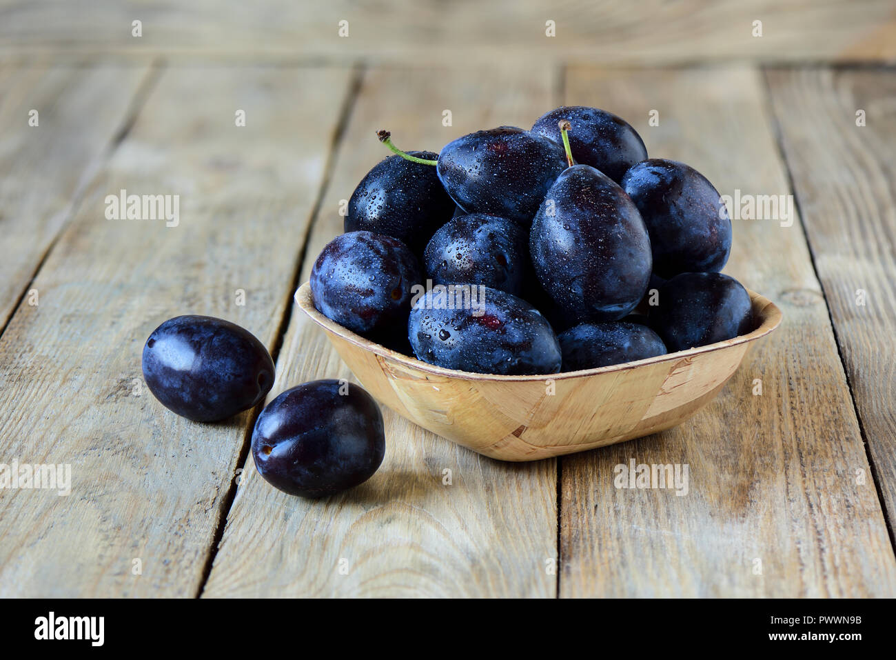 Ripe blue plums in a wooden bowl on a wooden background Stock Photo - Alamy