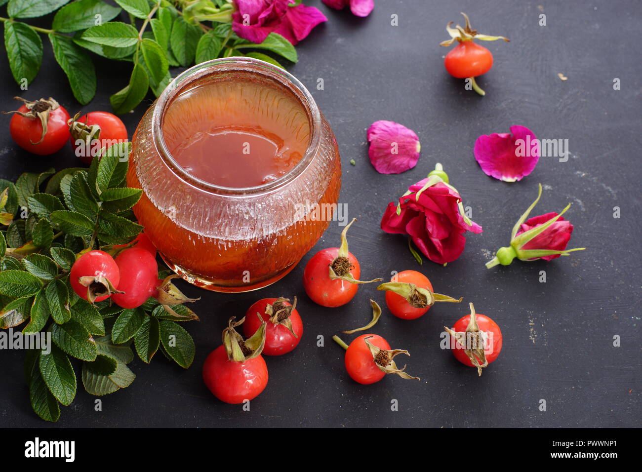 A jar of wild rose jam, next to a twig from the garden with berries and ...