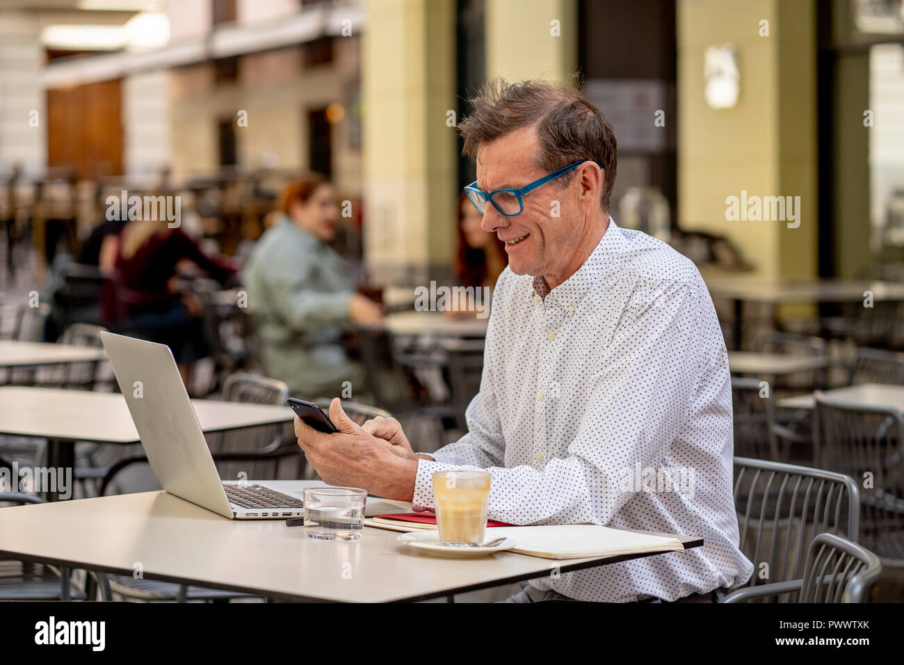 Smiling old man checking smart phone while working on computer in ...