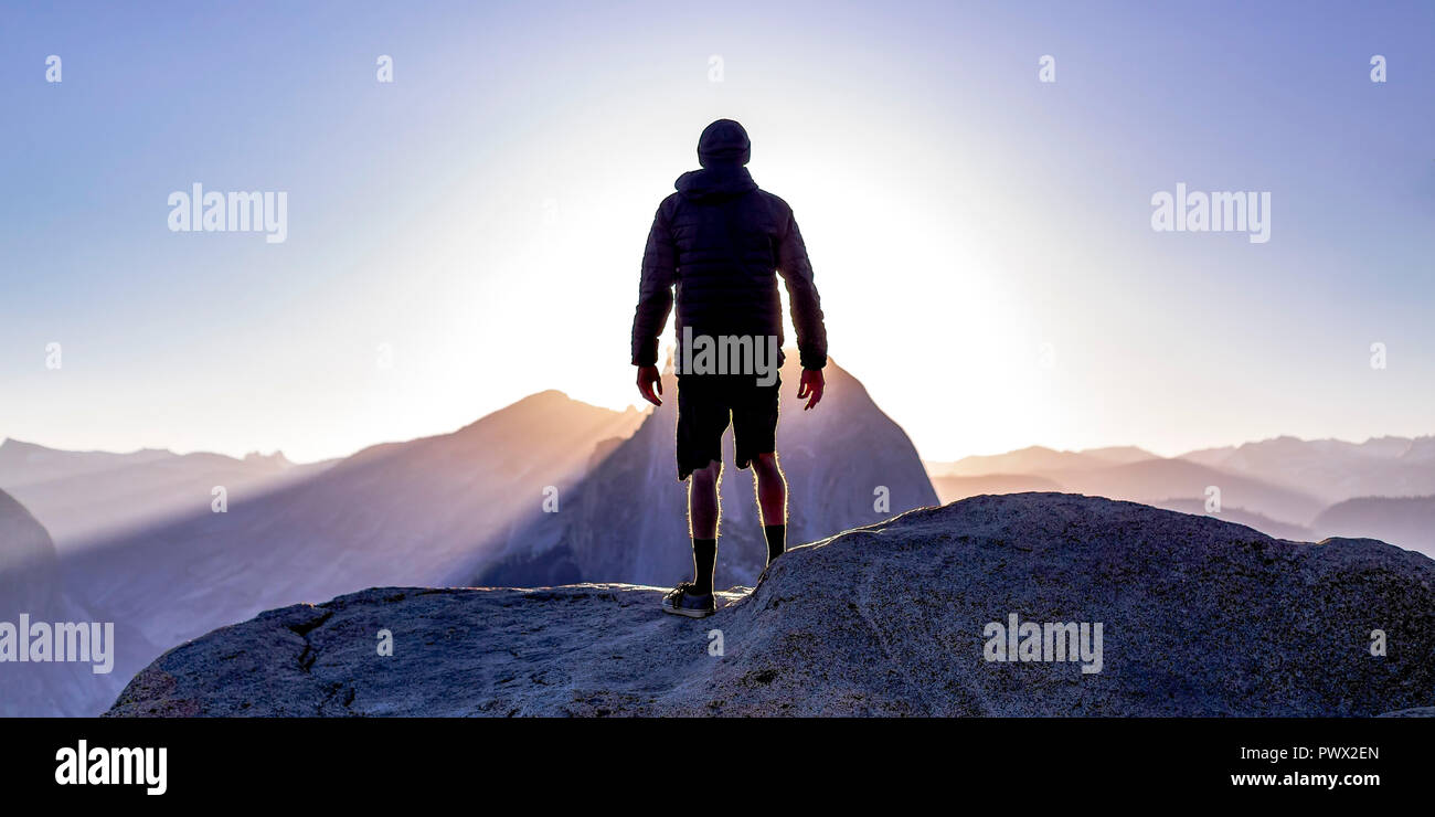 Man on a cliff with view of sun and mountains Stock Photo - Alamy
