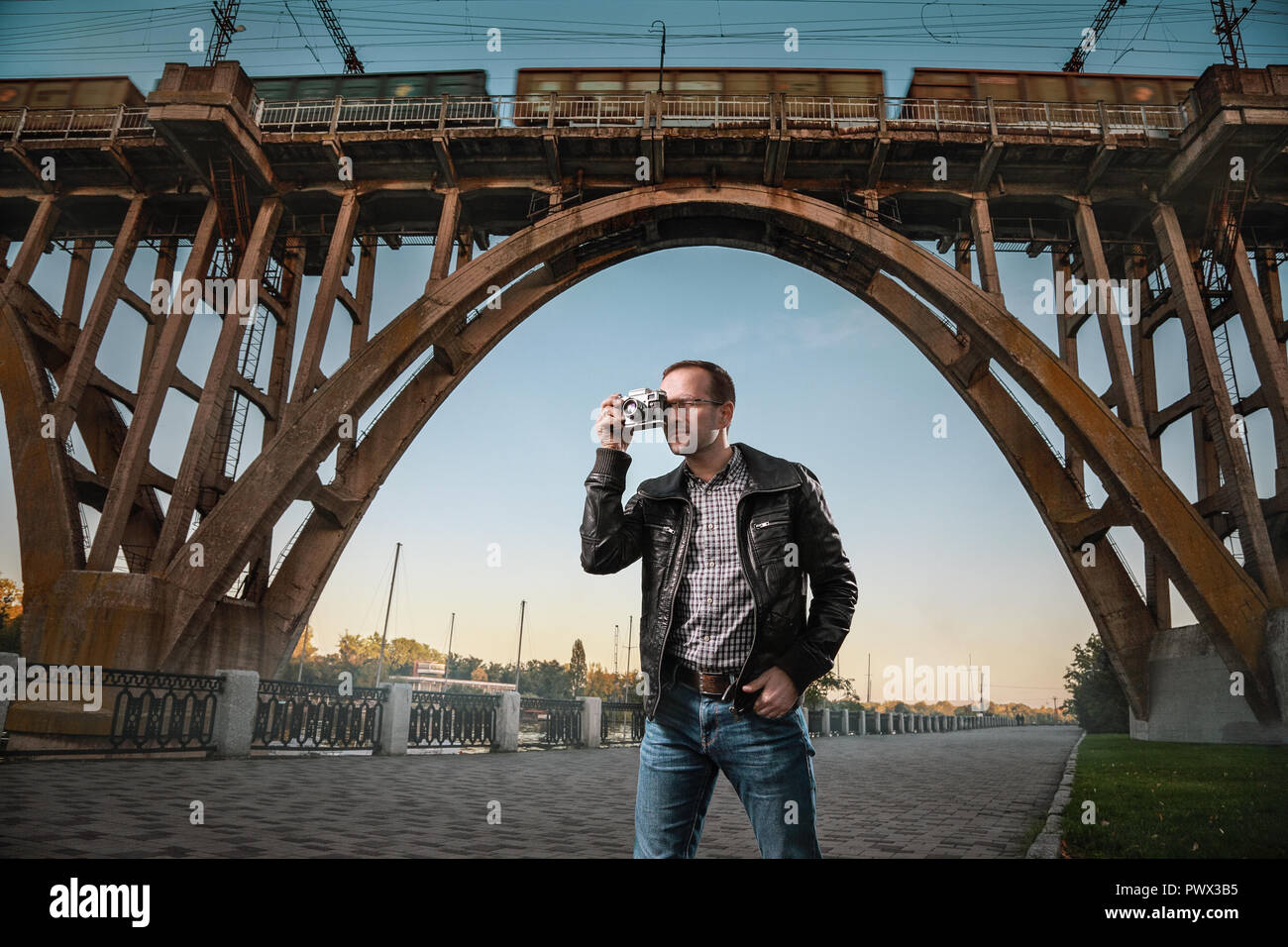 Man with a retro film camera walks around the city, under the bridge ...