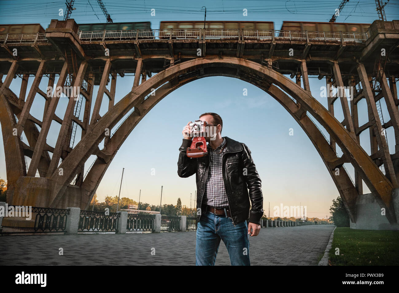 Man with a retro film camera walks around the city, under the bridge ...