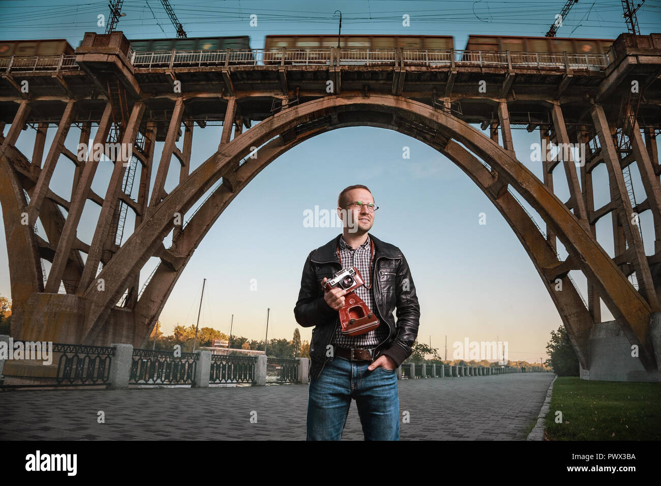Man with a retro film camera walks around the city, under the bridge ...