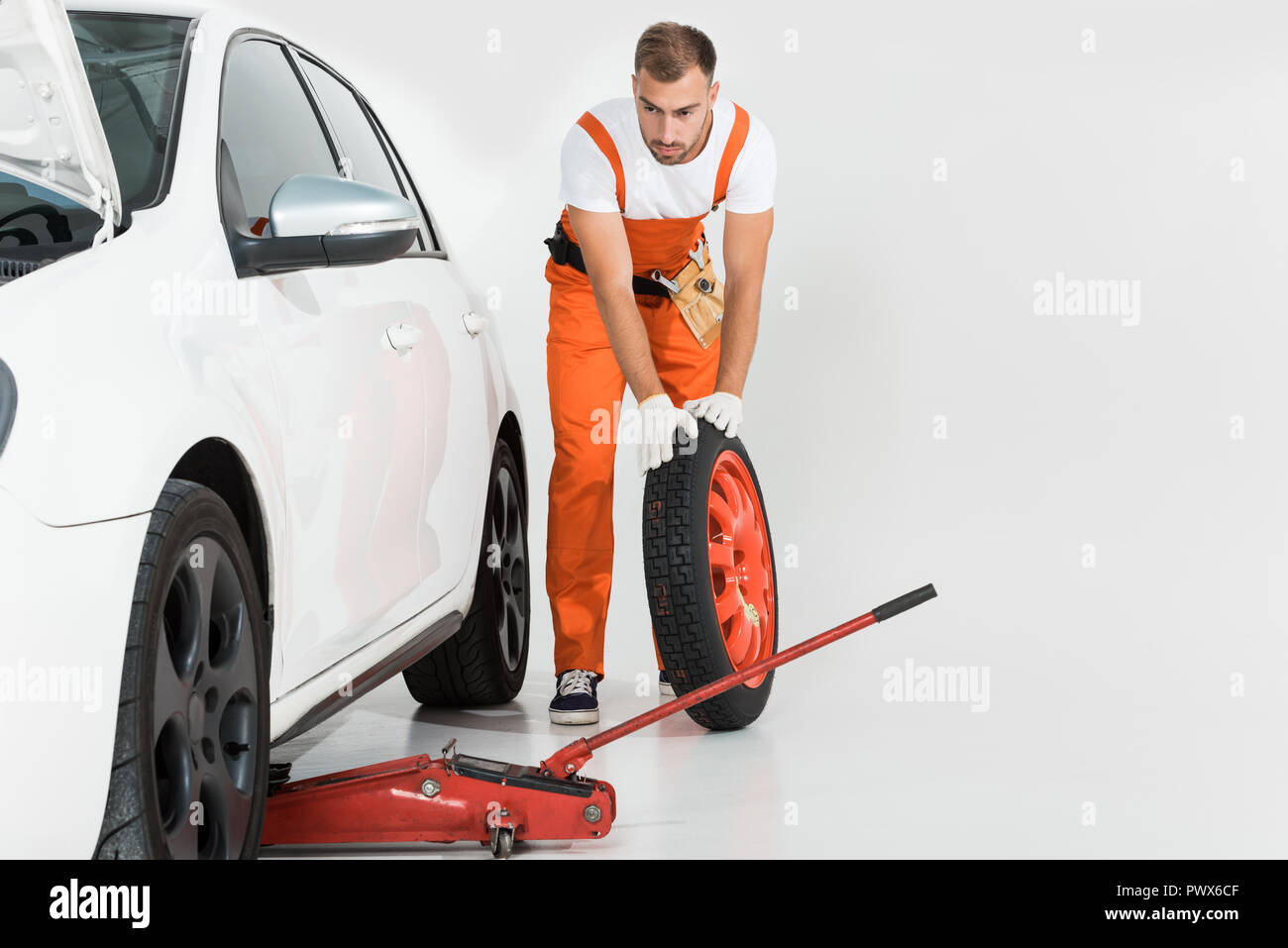 auto mechanic rolling tire to car on white Stock Photo - Alamy