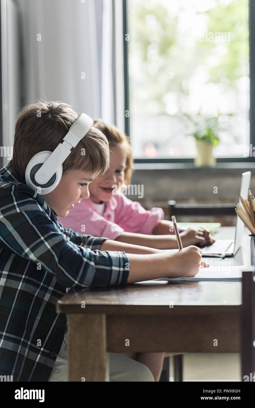 side view of little schoolboy drawing with color pencils while his ...