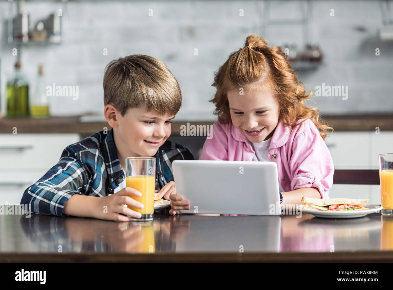 smiling little brother and sister using tablet during breakfast Stock ...