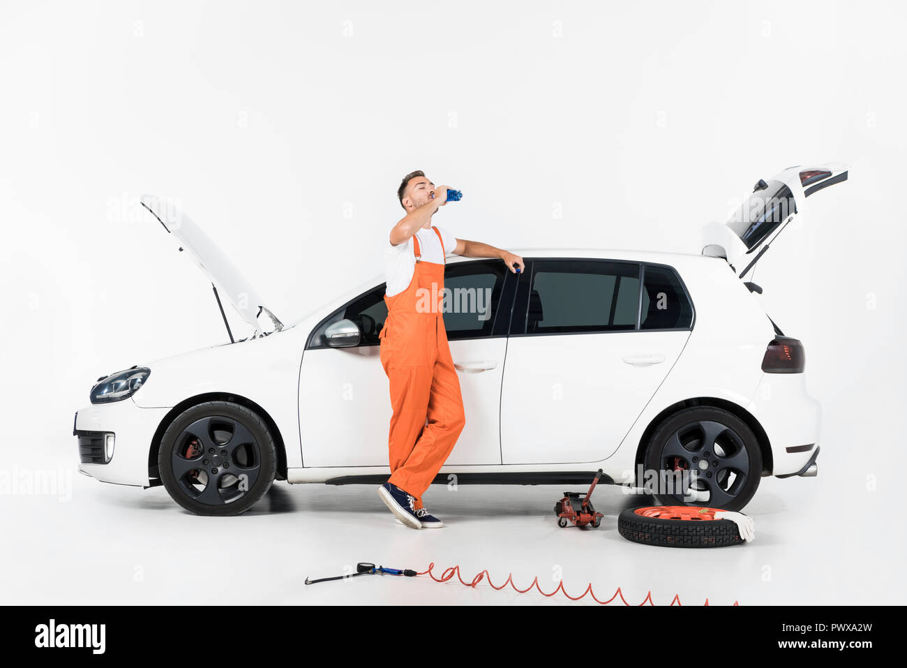 handsome auto mechanic drinking water and leaning on car on white Stock ...