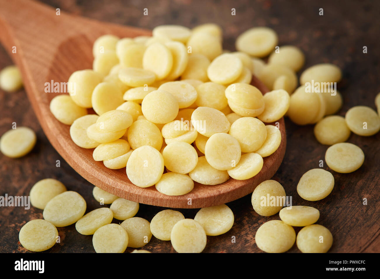 Organic cacao butter buttons (wafers) in wooden spoon on rustic ...