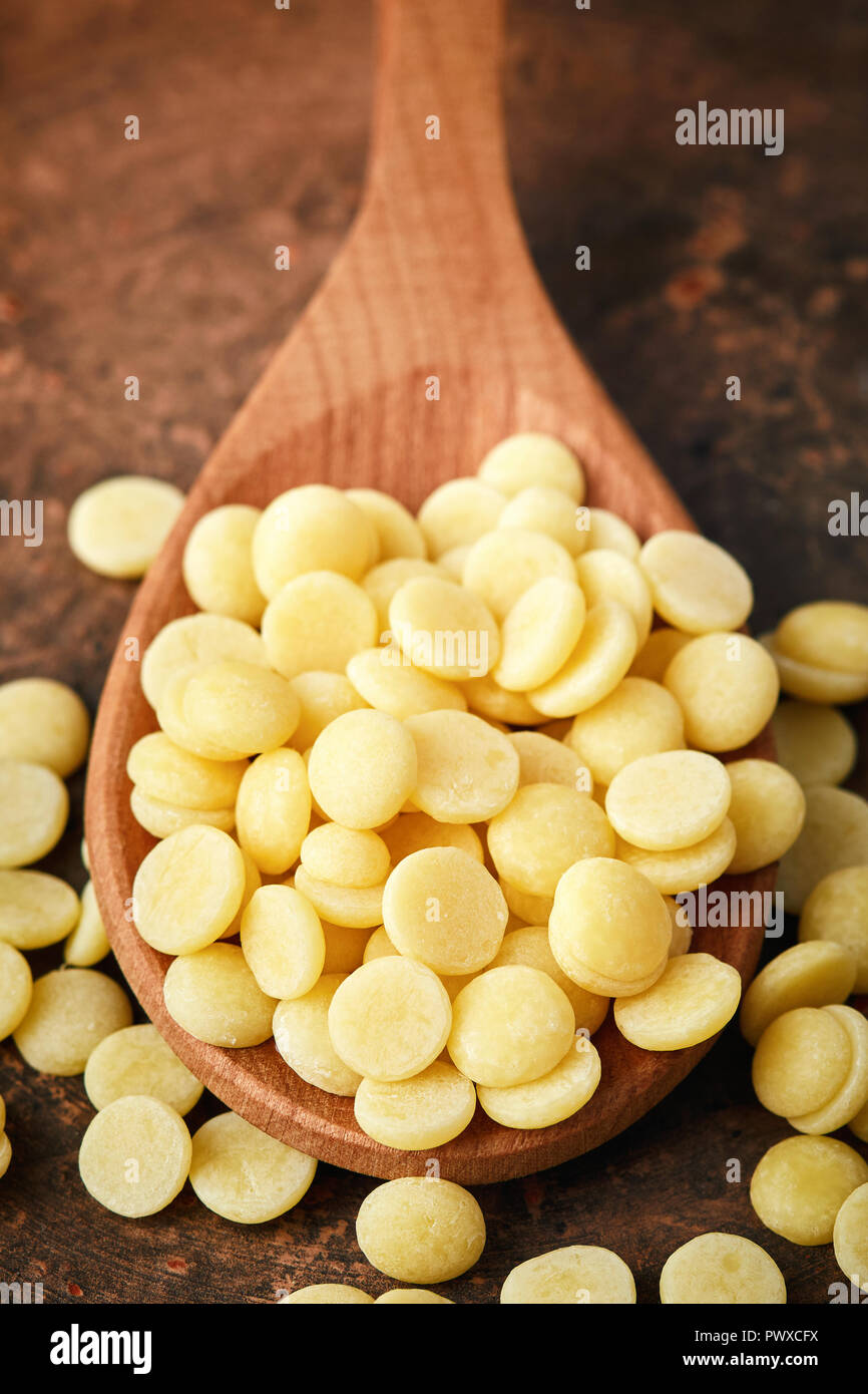 Organic cacao butter buttons (wafers) in wooden spoon on rustic ...
