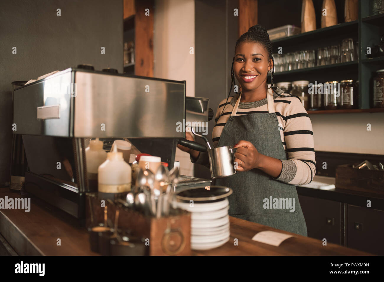 Smiling young African barista preparing coffee behind a cafe counter ...