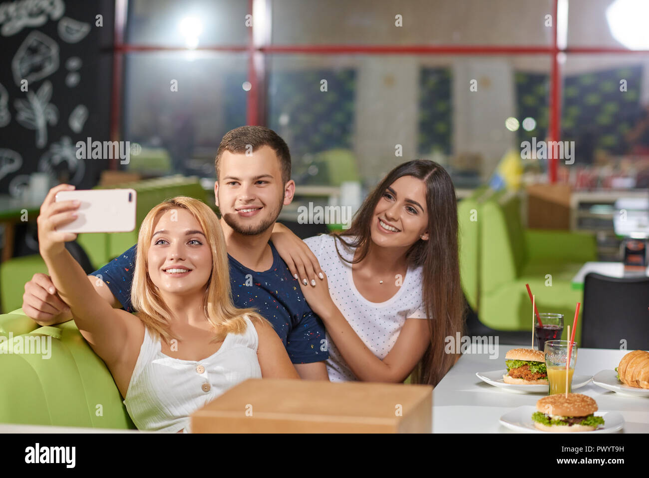 Happy company taking selfie while eating tasty fast food in cafe ...