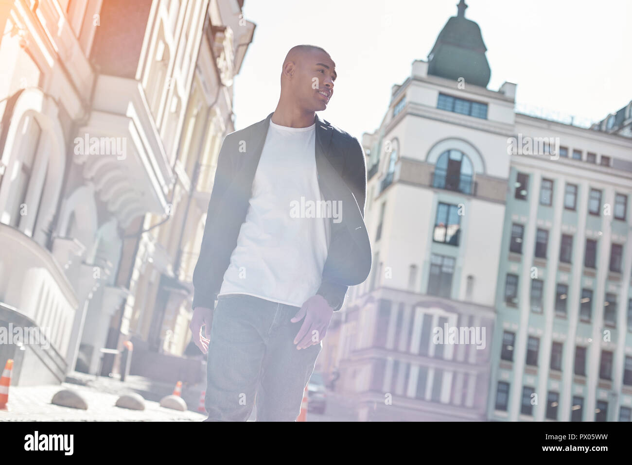 City walk. Young man walking on the street looking aside smiling joyful ...