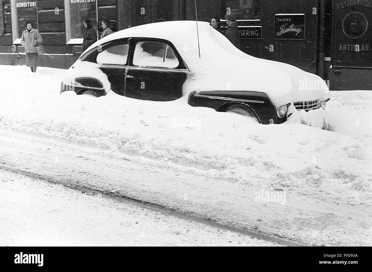 Winter driving in the 1950s. Snow has fallen heavily and the car parked ...