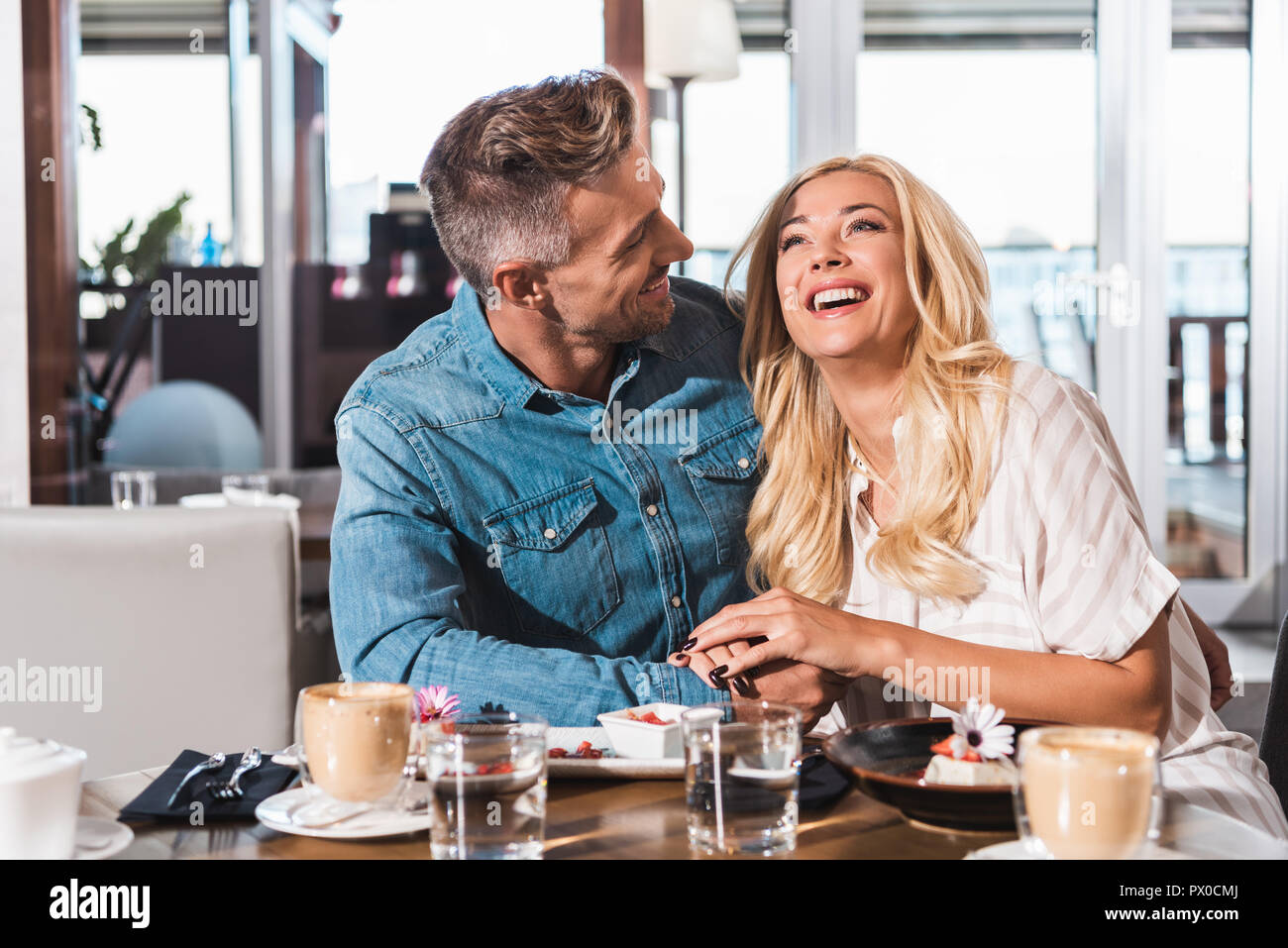 handsome boyfriend looking at laughing girlfriend at table in cafe ...