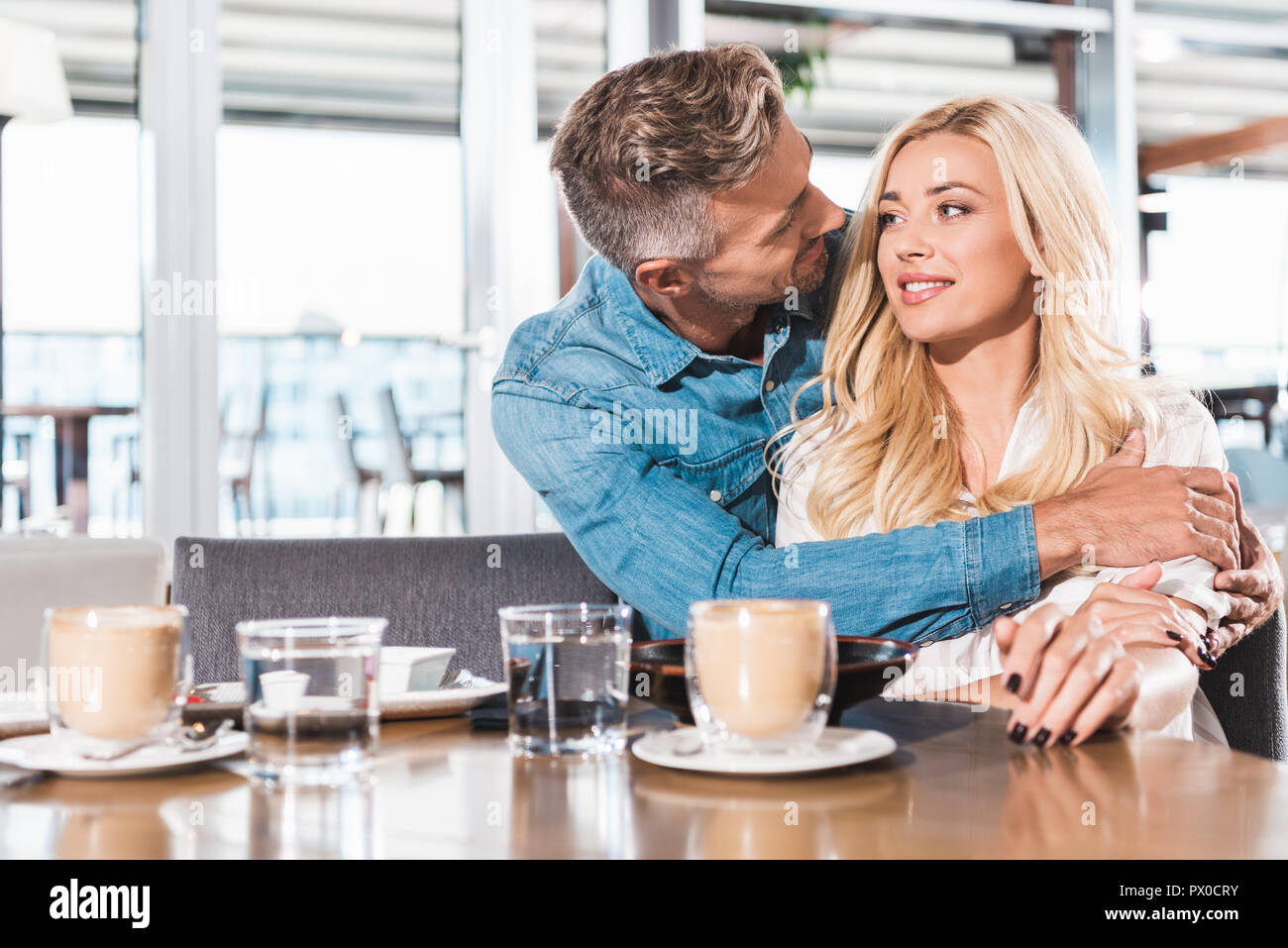 handsome boyfriend cuddling attractive girlfriend at table in cafe ...