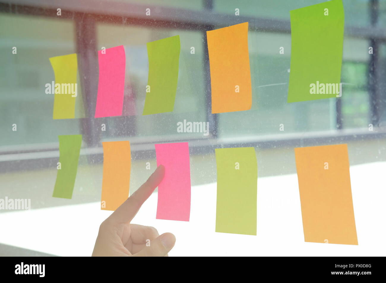 hand pointing at adhesive notes on glass wall at workplace. Sticky note ...