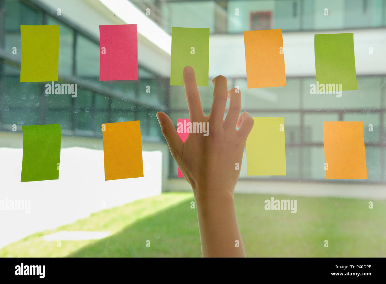 hand pointing at adhesive notes on glass wall at workplace. Sticky note ...