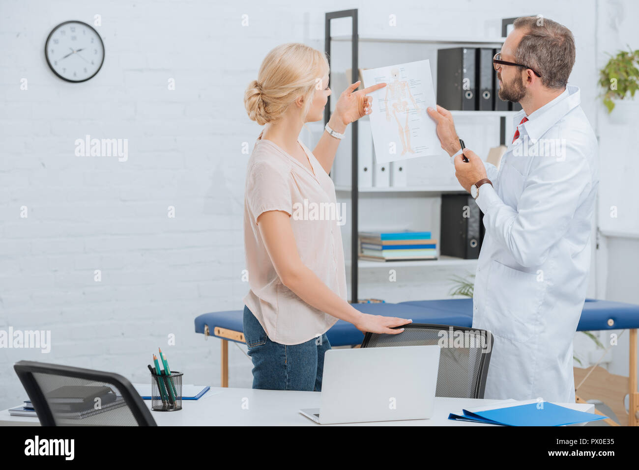 chiropractic in white coat showing human body scheme to female patient ...