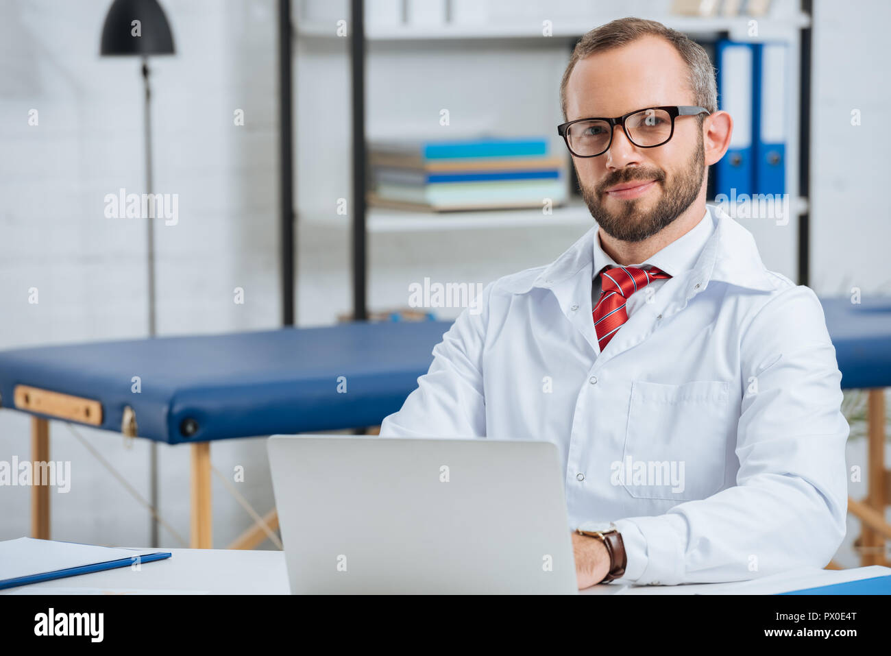portrait of smiling male chiropractor in white coat at workplace with ...