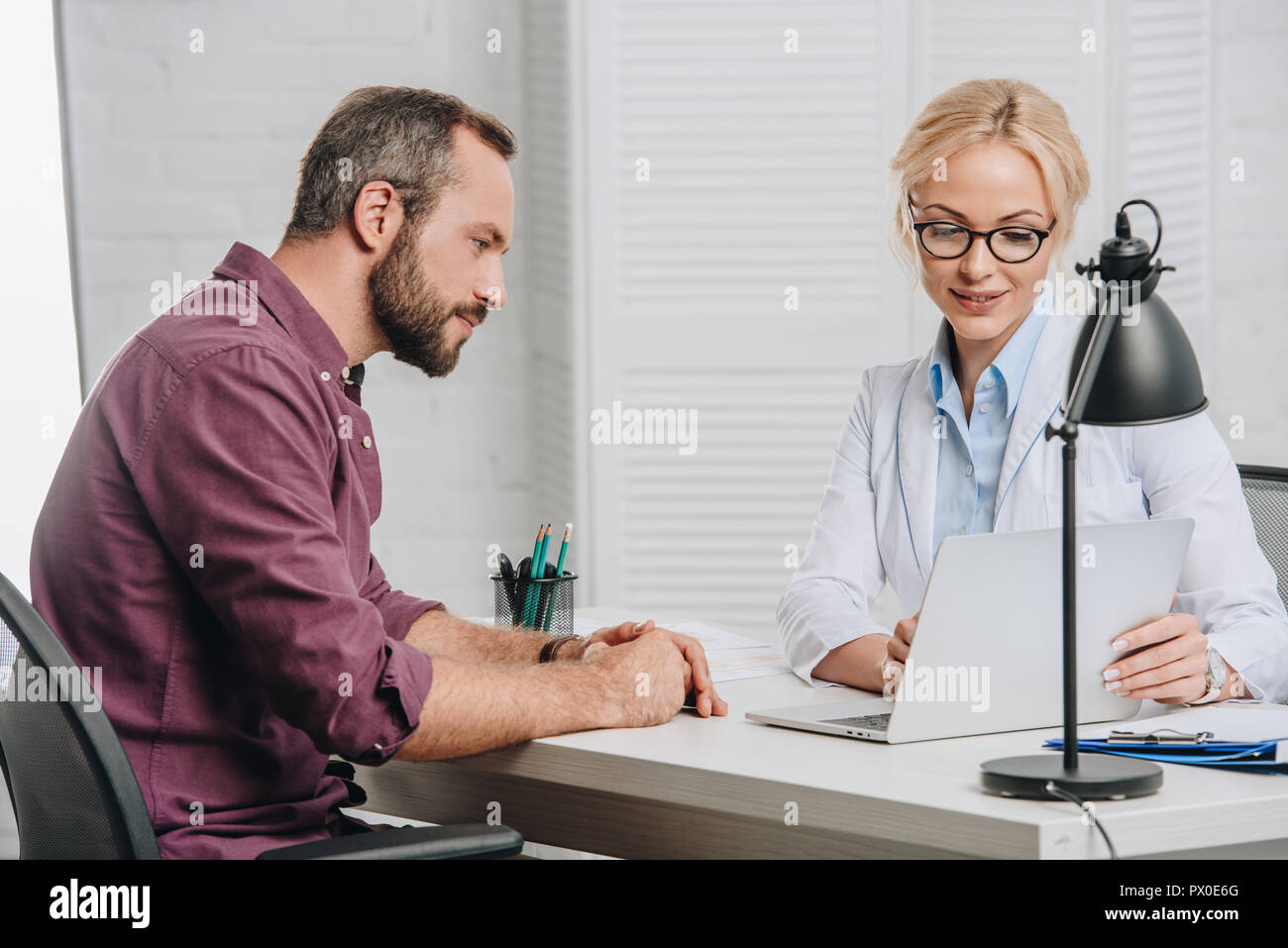 side view of female chiropractor pointing at laptop screen during ...