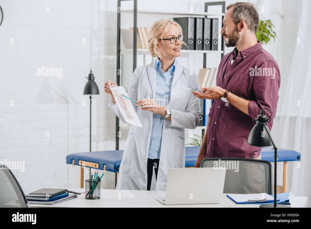 female physiotherapist showing human body picture to patient in clinic ...