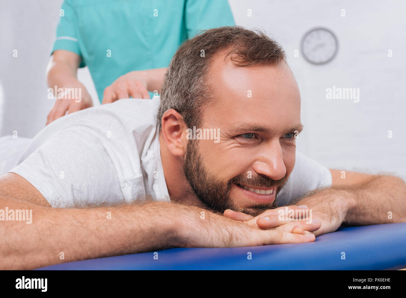 partial view of massage therapist doing massage to smiling patient on ...