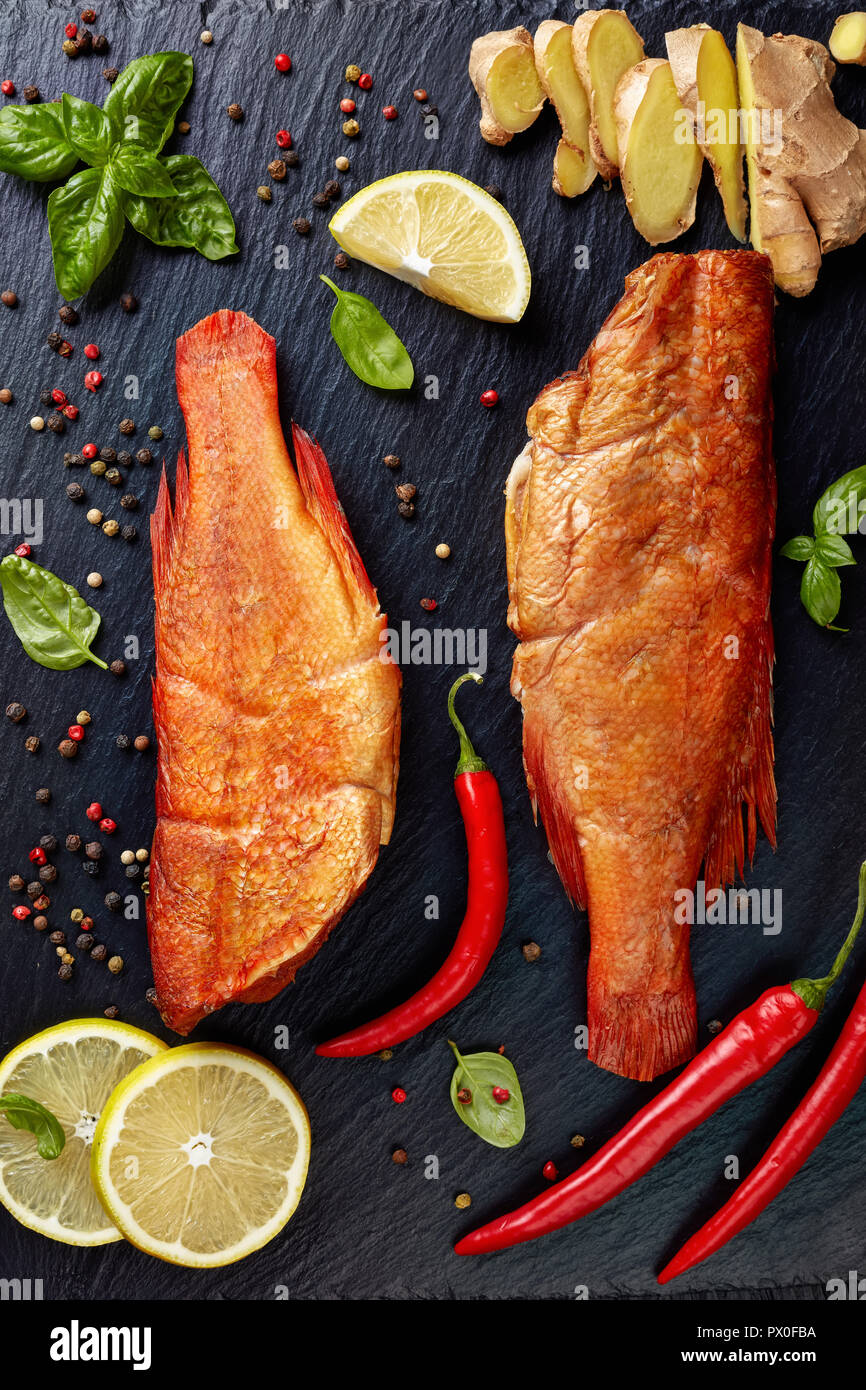 hot smoked red snappers on a black stone plate with spices, herbs and ...