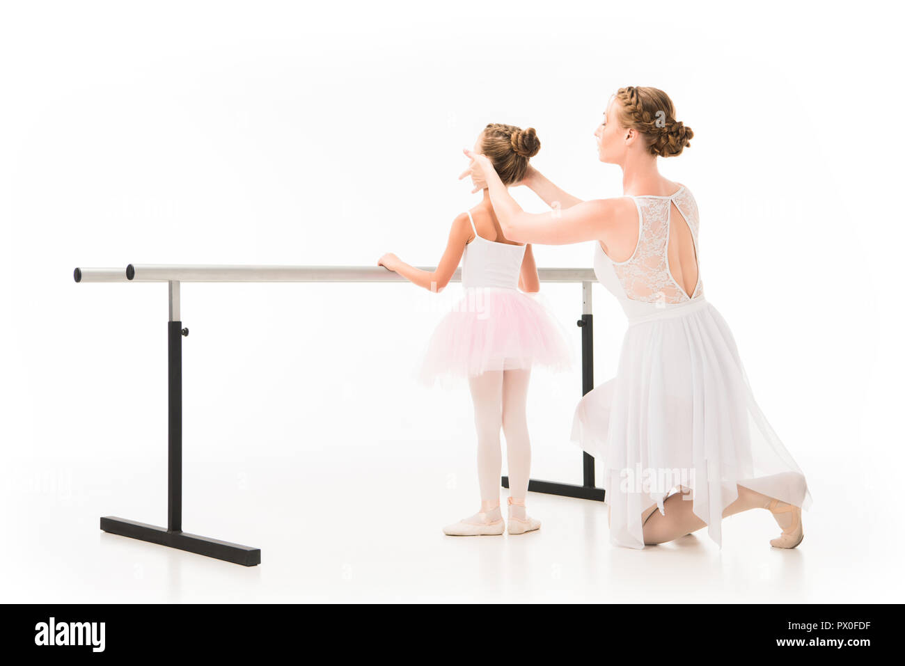 rear view of adult female teacher in tutu helping little ballerina ...