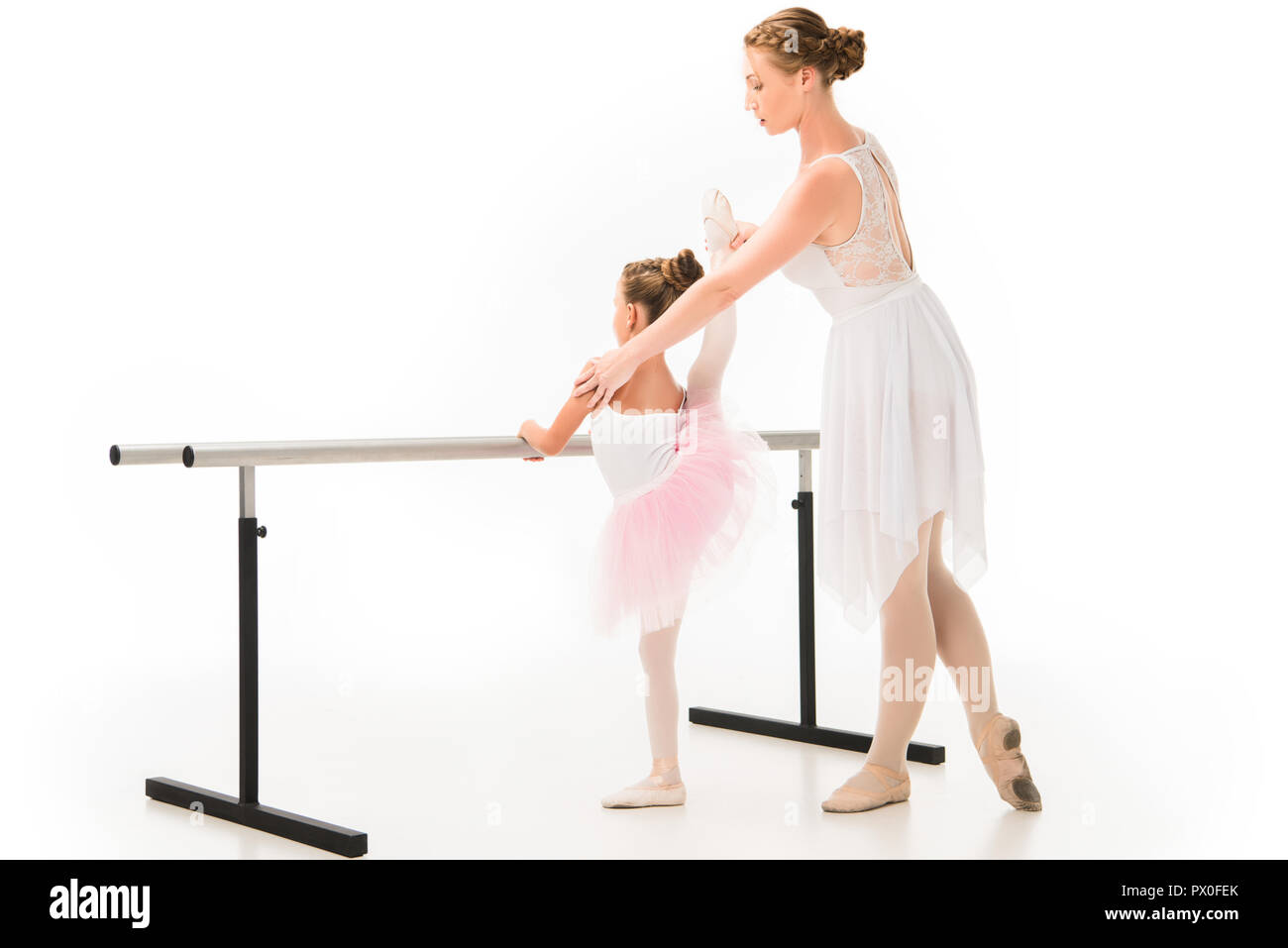 side view of female teacher in tutu helping little ballerina practicing ...