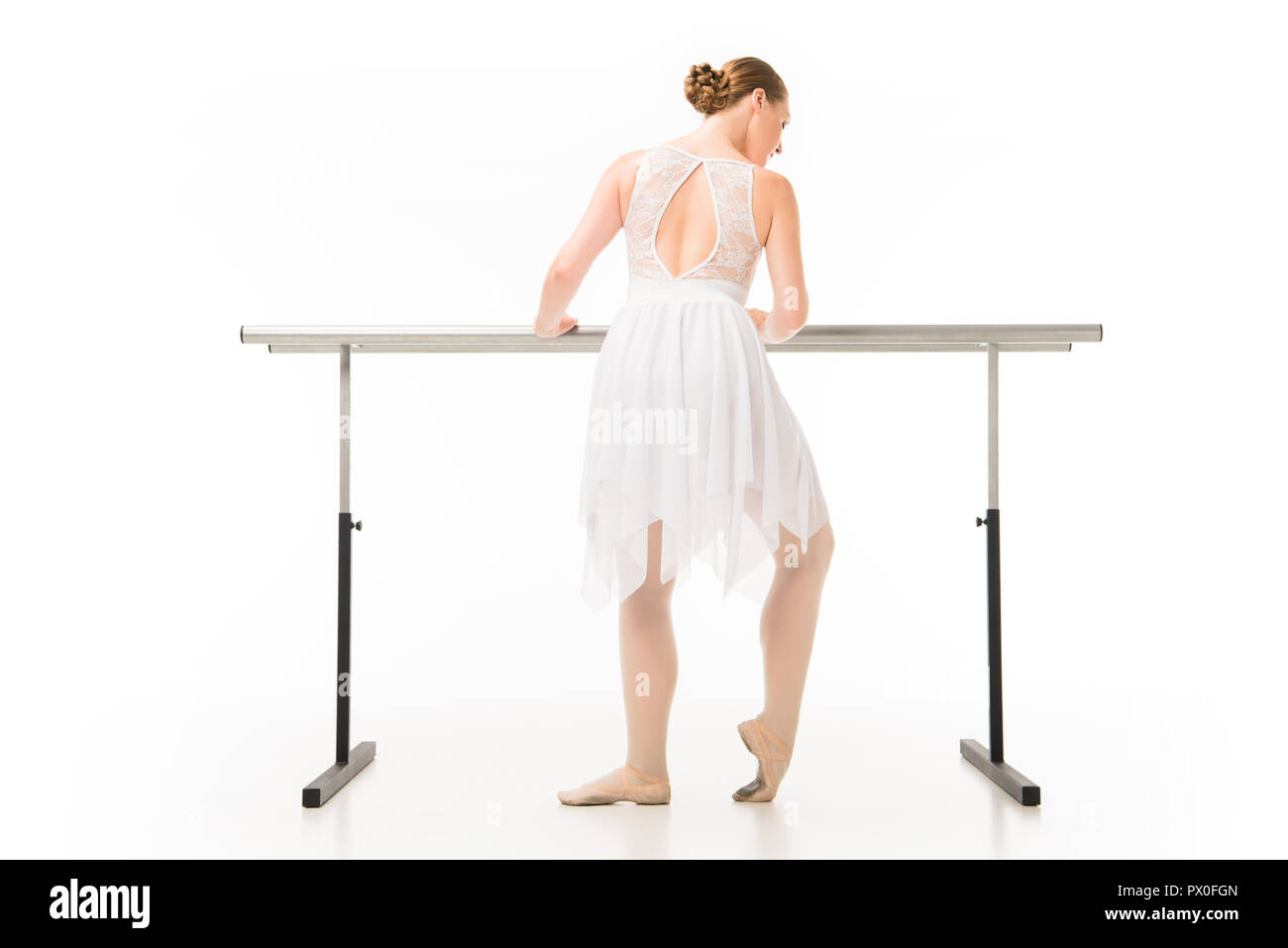 rear view of adult ballerina in tutu exercising at ballet barre stand ...