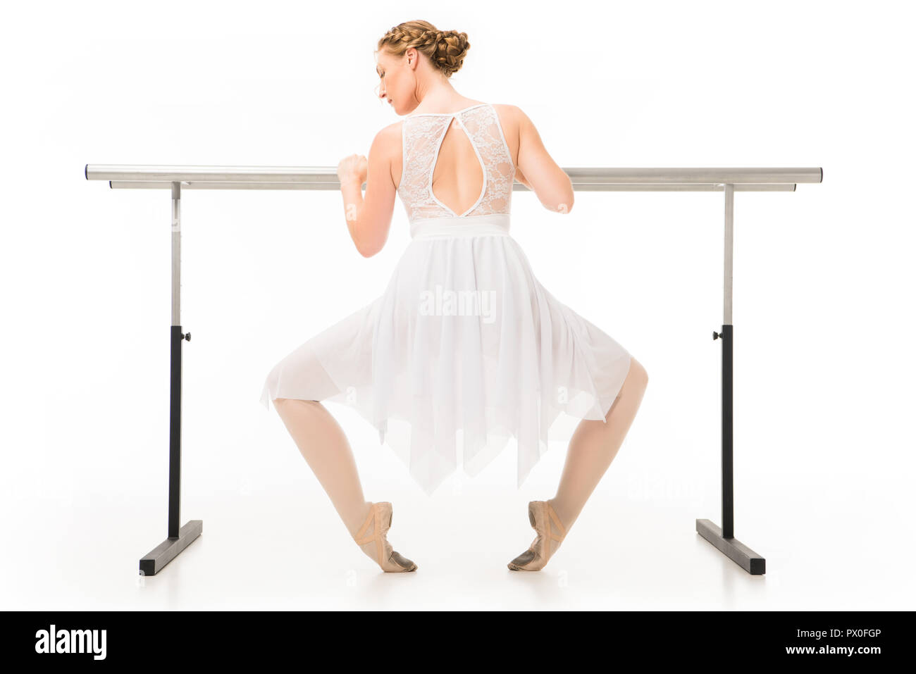 rear view of attractive ballerina in tutu exercising at ballet barre ...