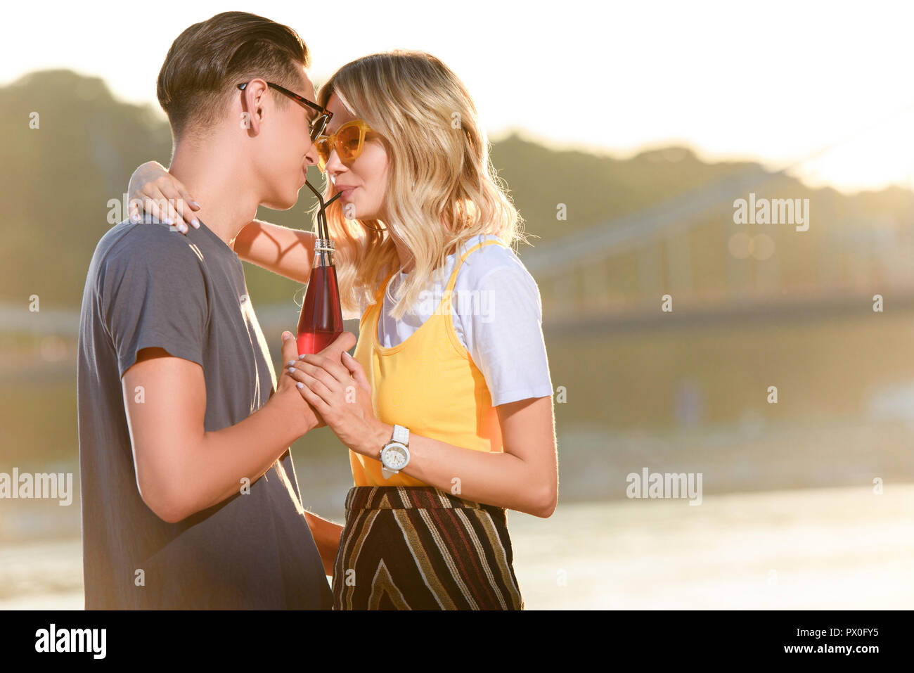 couple hugging and drinking beverage with two plastic straws from one ...