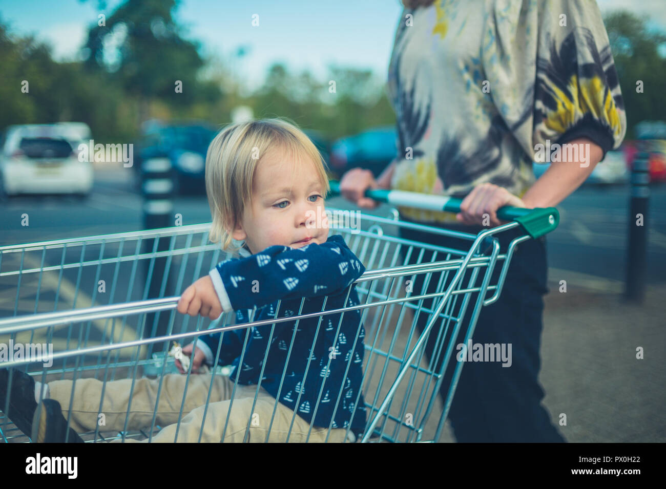 A little toddler is being pushed around in a shopping trolley by his ...