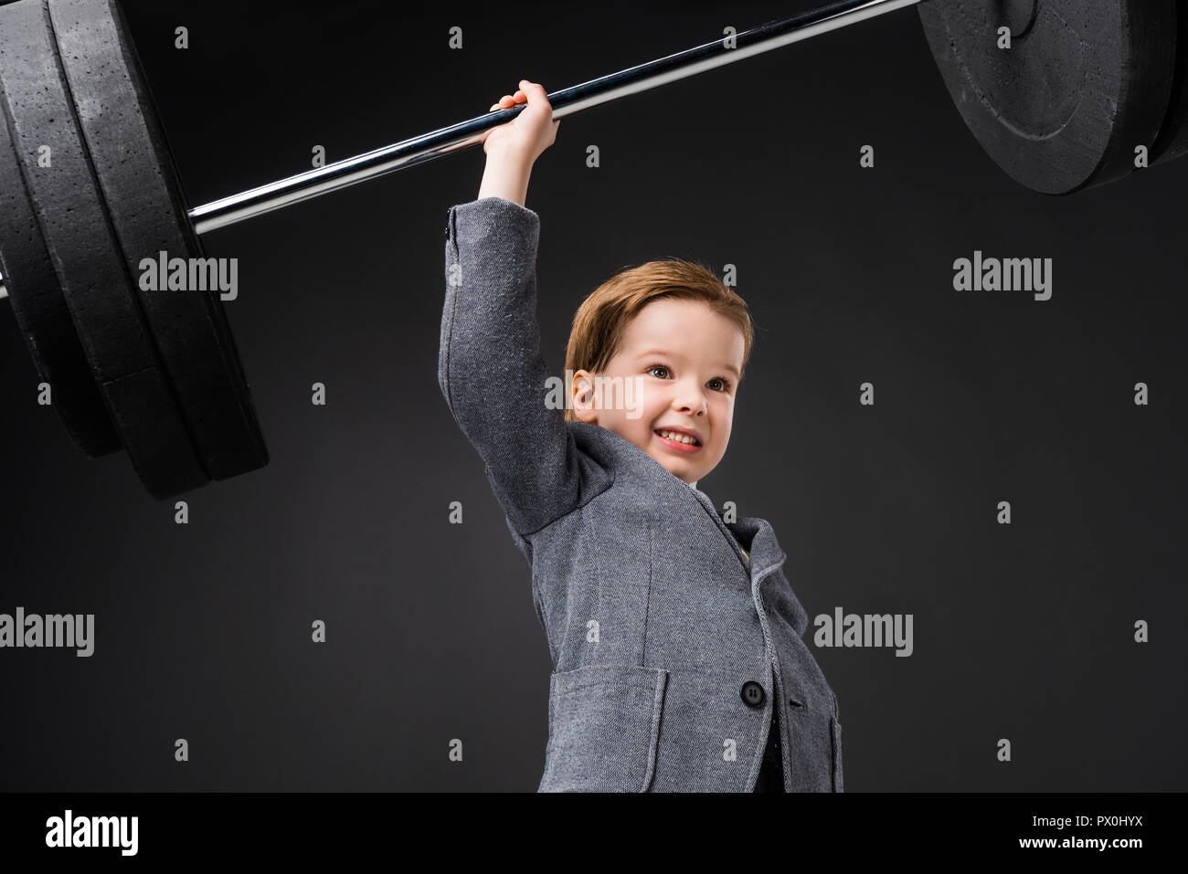 strong cheerful boy in suit lifting barbell isolated on grey Stock ...