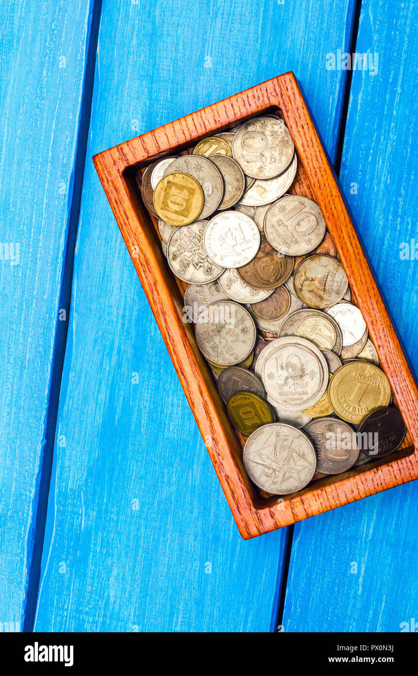 box with coins of countries of the world on a blue wooden background ...