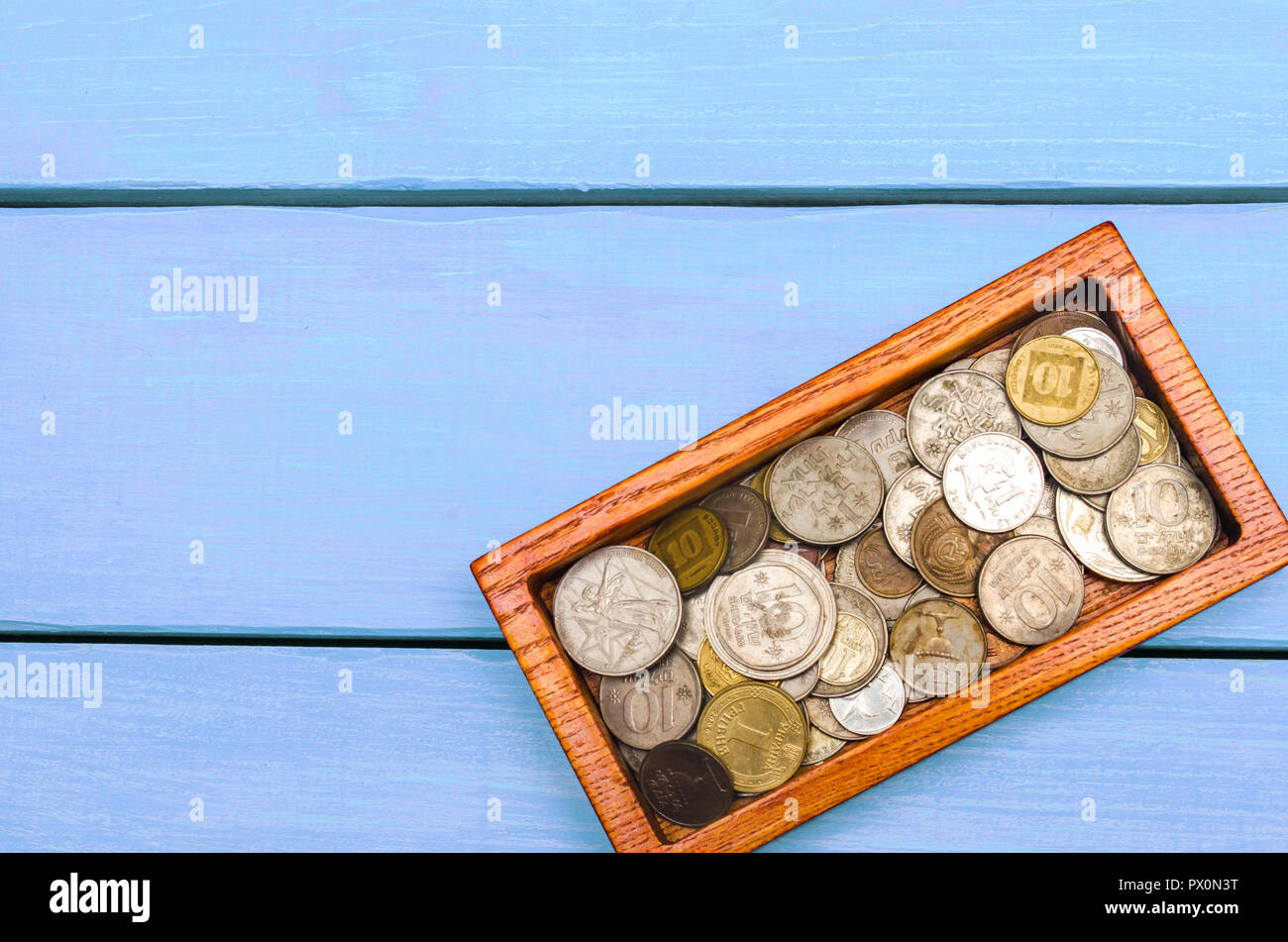box with coins of countries of the world on a blue wooden background ...