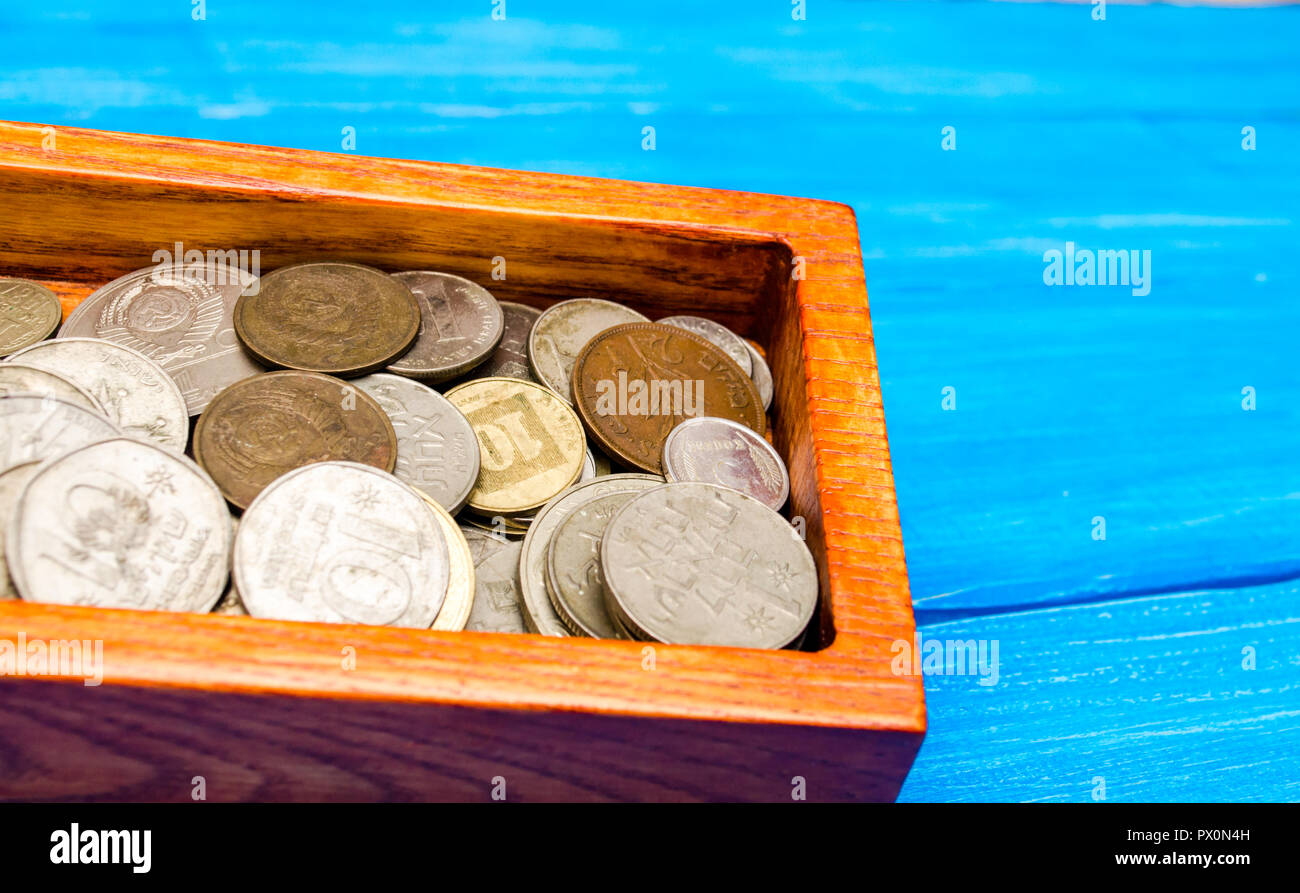 box with coins of countries of the world on a blue wooden background ...