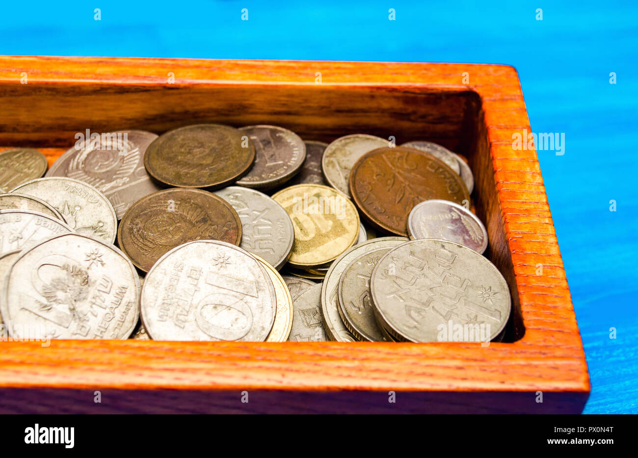 box with coins of countries of the world on a blue wooden background ...