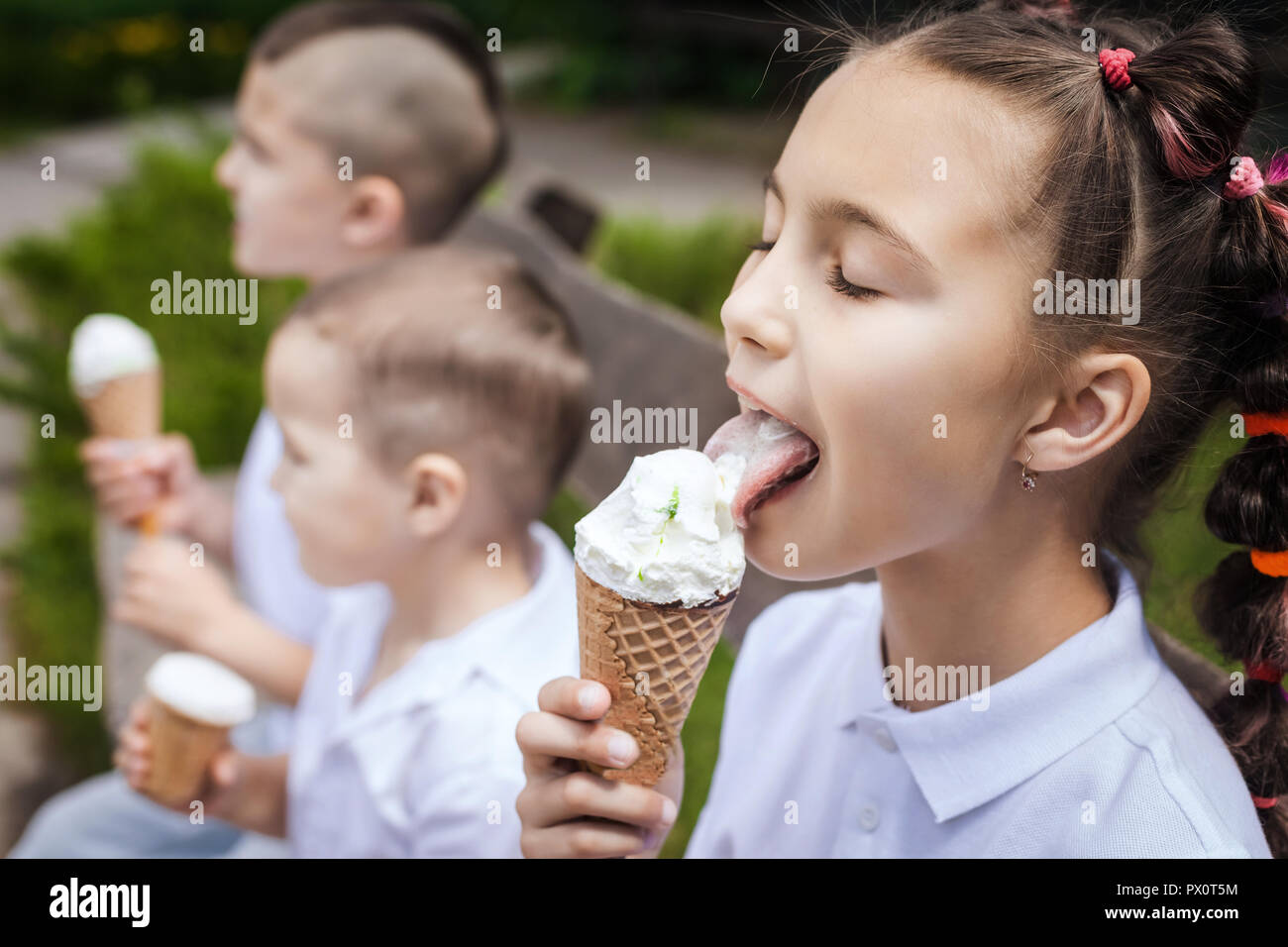 adorable lovely children eating ice cream sitting on a wooden bench in ...
