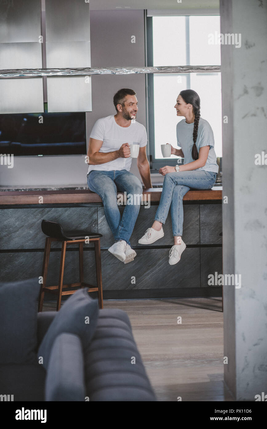 couple sitting on kitchen counter with cups of coffee in morning Stock ...