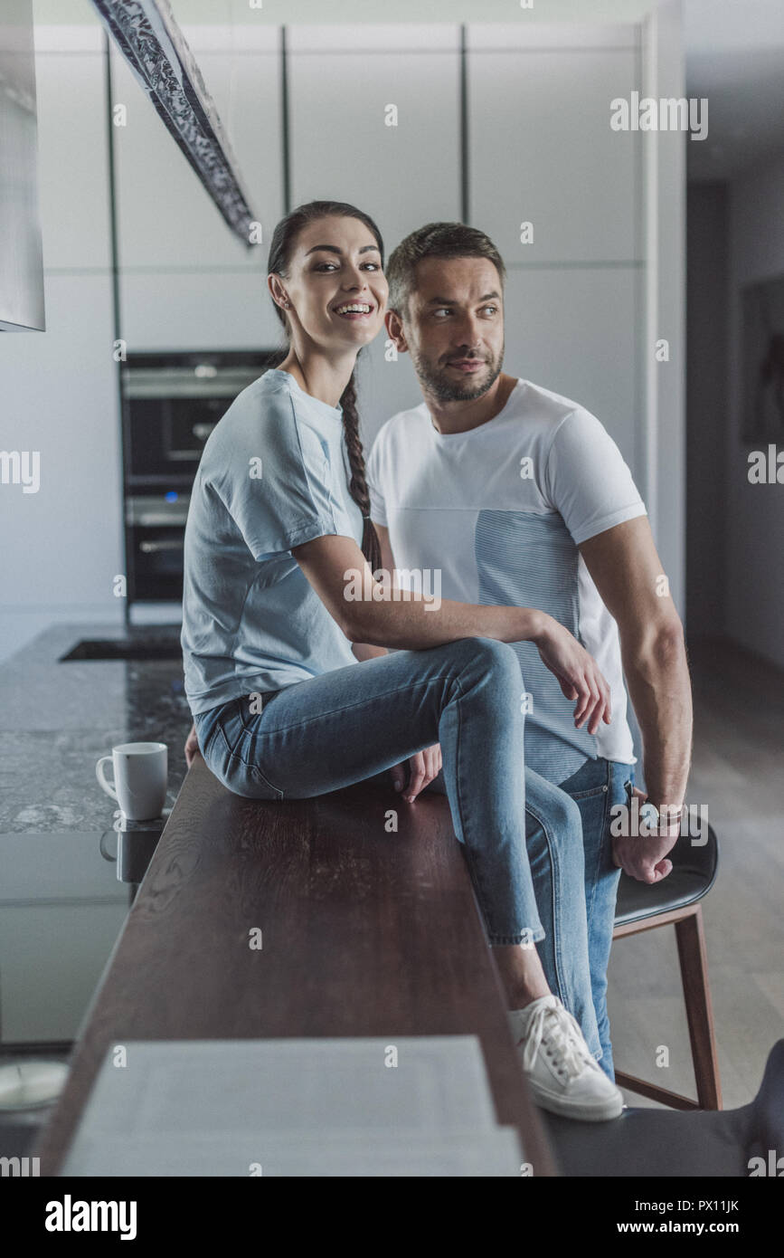 happy young woman sitting on kitchen counter while her boyfriend ...