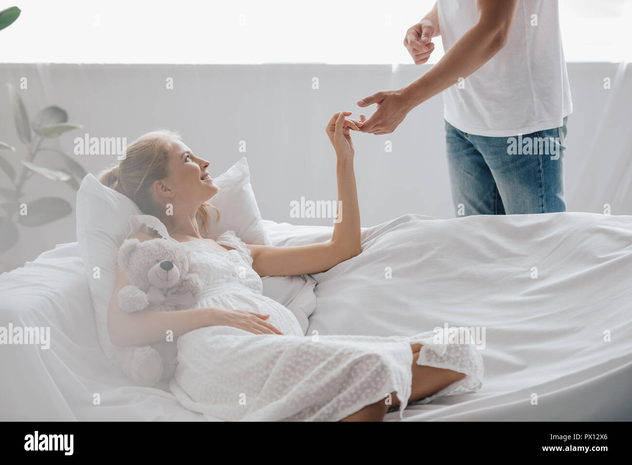 man and pregnant wife in white nightie on sofa holding hands at home ...