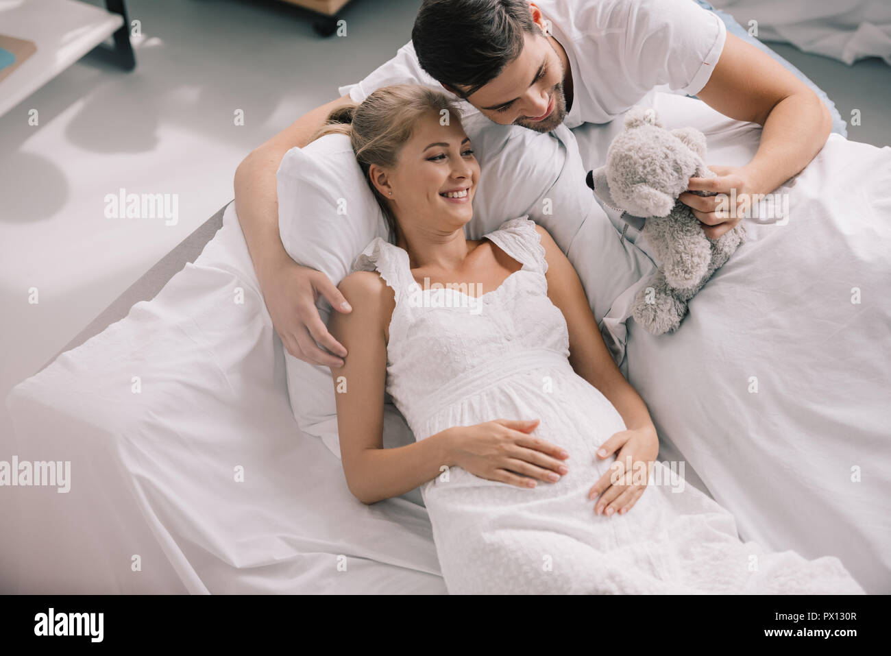 high angle view of man with teddy bear near smiling pregnant wife in ...