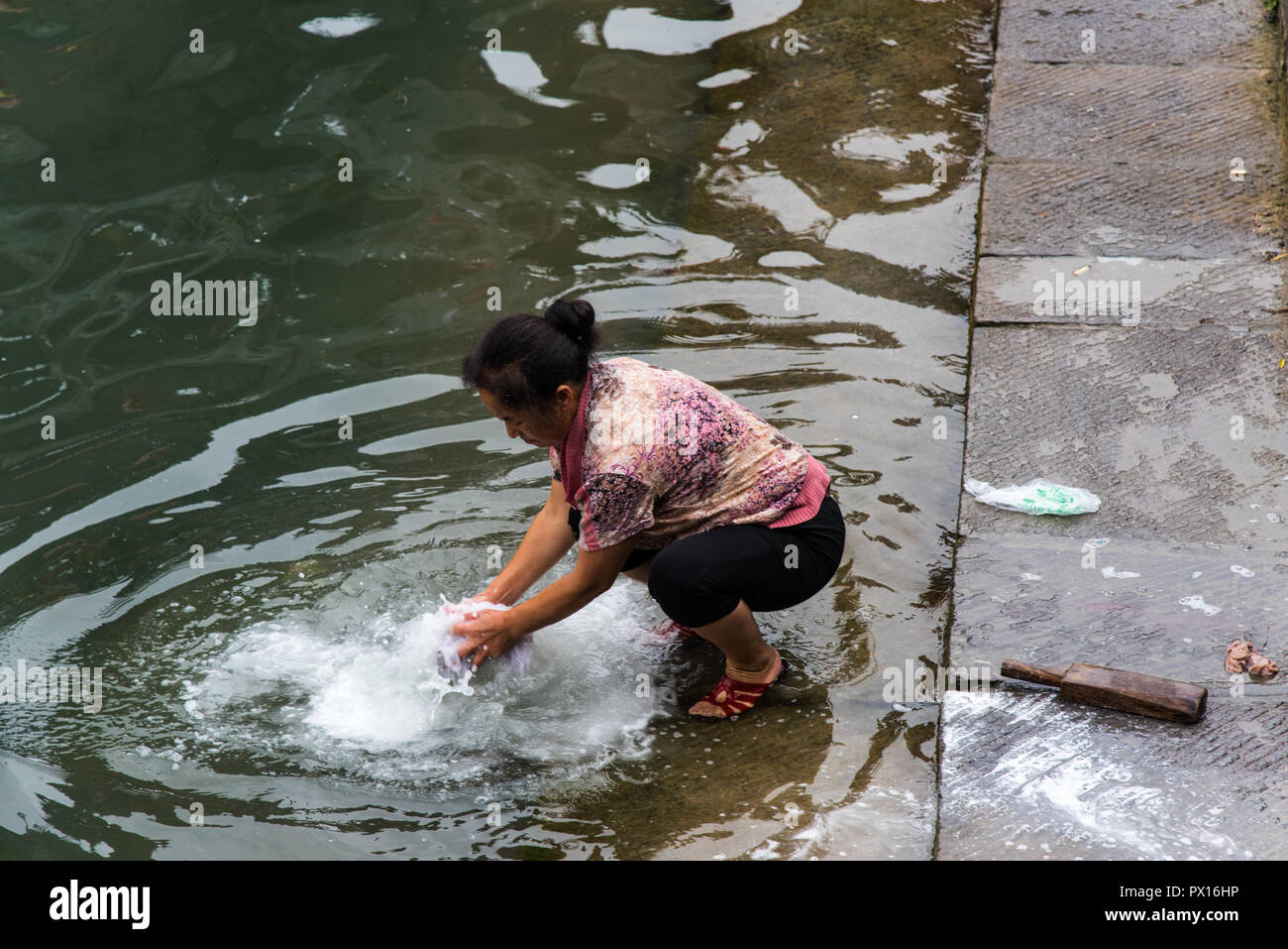 FENGHUANG, HUNAN, CHINA - 8JUL2018: Woman washing clothes in the ...