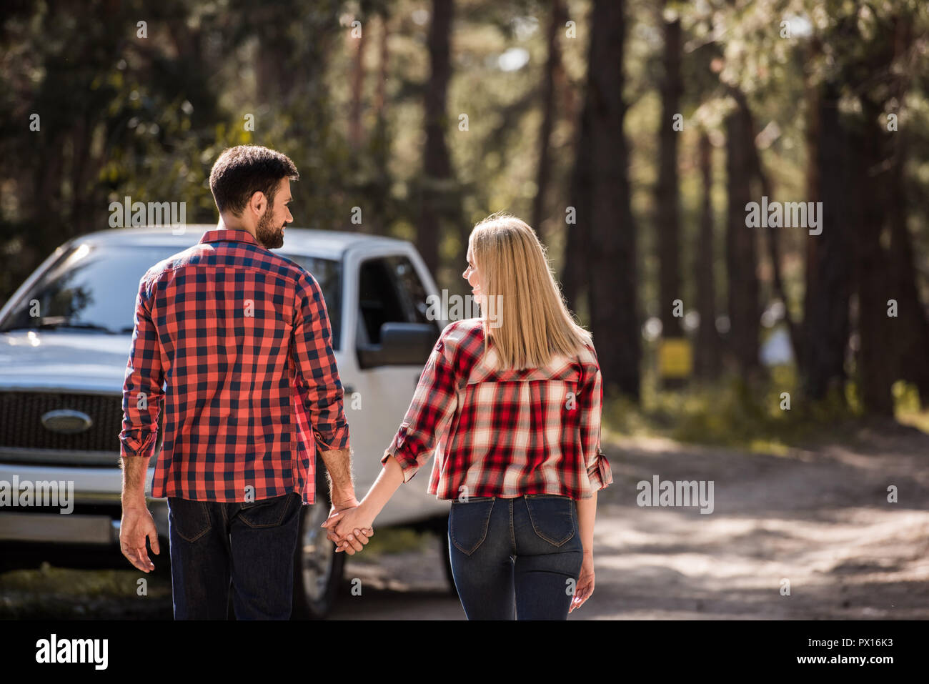 back view of couple holding hands and going to pickup truck in forest ...
