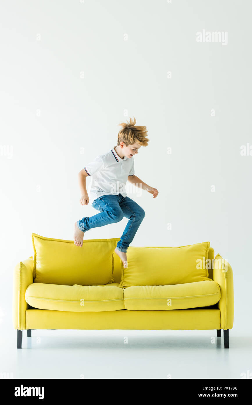 adorable boy in casual clothes jumping on yellow sofa on white Stock ...