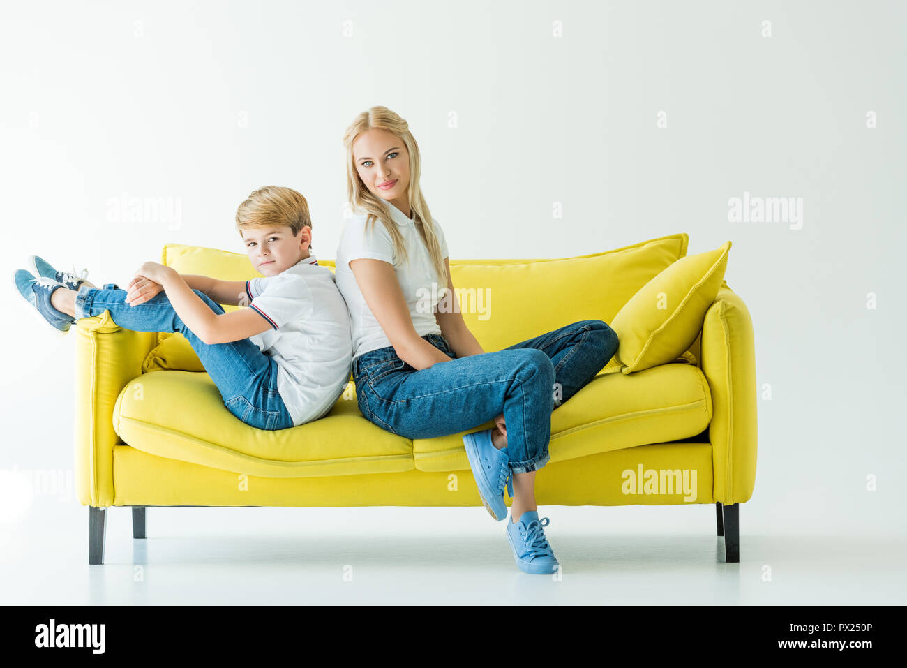 mother and son sitting back to back on yellow sofa on white Stock Photo ...