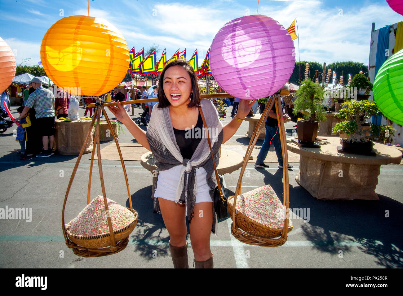A Vietnamese American young adult laughs as she balances two baskets of ...