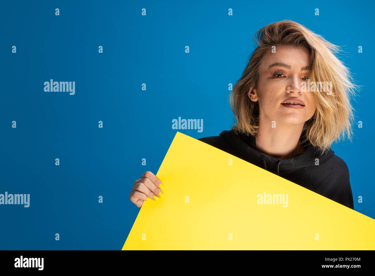 Pretty young woman displaying a yellow cardboard advertising sign ...
